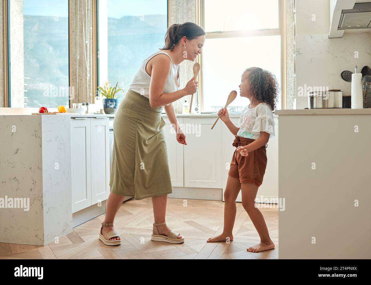 Mother and little daughter singing karaoke and dancing in the kitchen ...