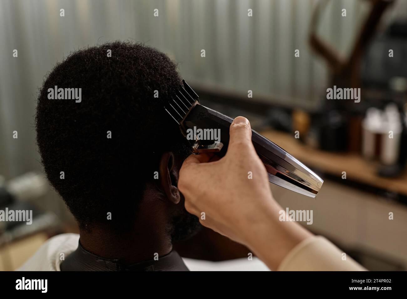 Rear view of customer sitting in chair while barber using trimmer to ...