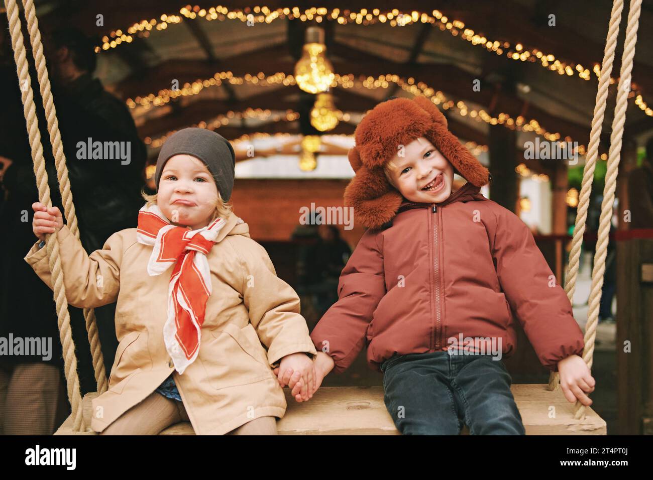 Outdoor portrait of two happy little kids sitting on swing at christmas ...