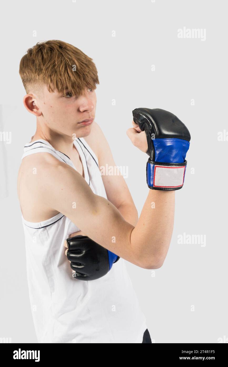 A caucasian teenage boy wearing MMA style boxing gloves punching upper ...