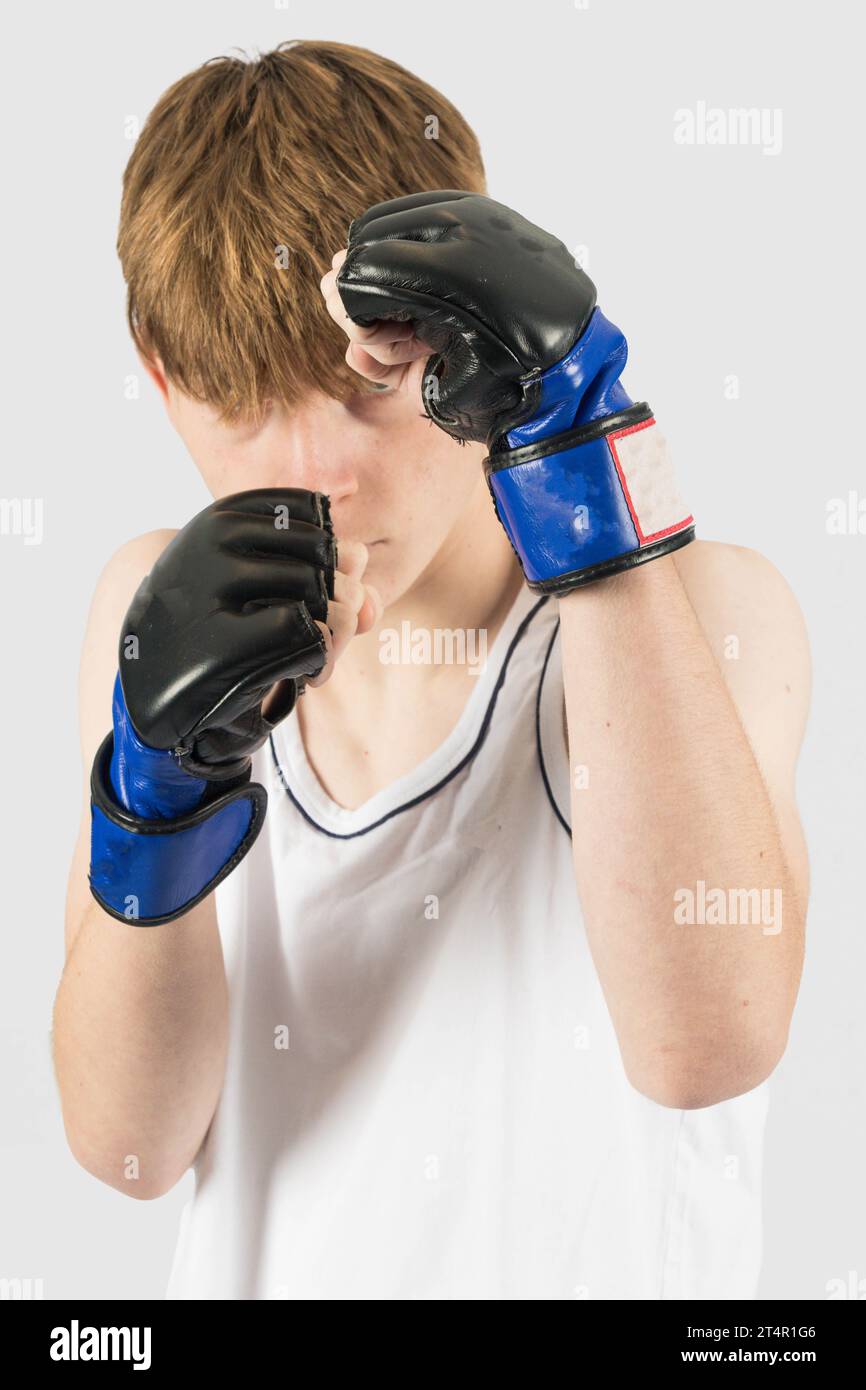 A caucasian teenage boy wearing MMA style boxing gloves with his guard ...