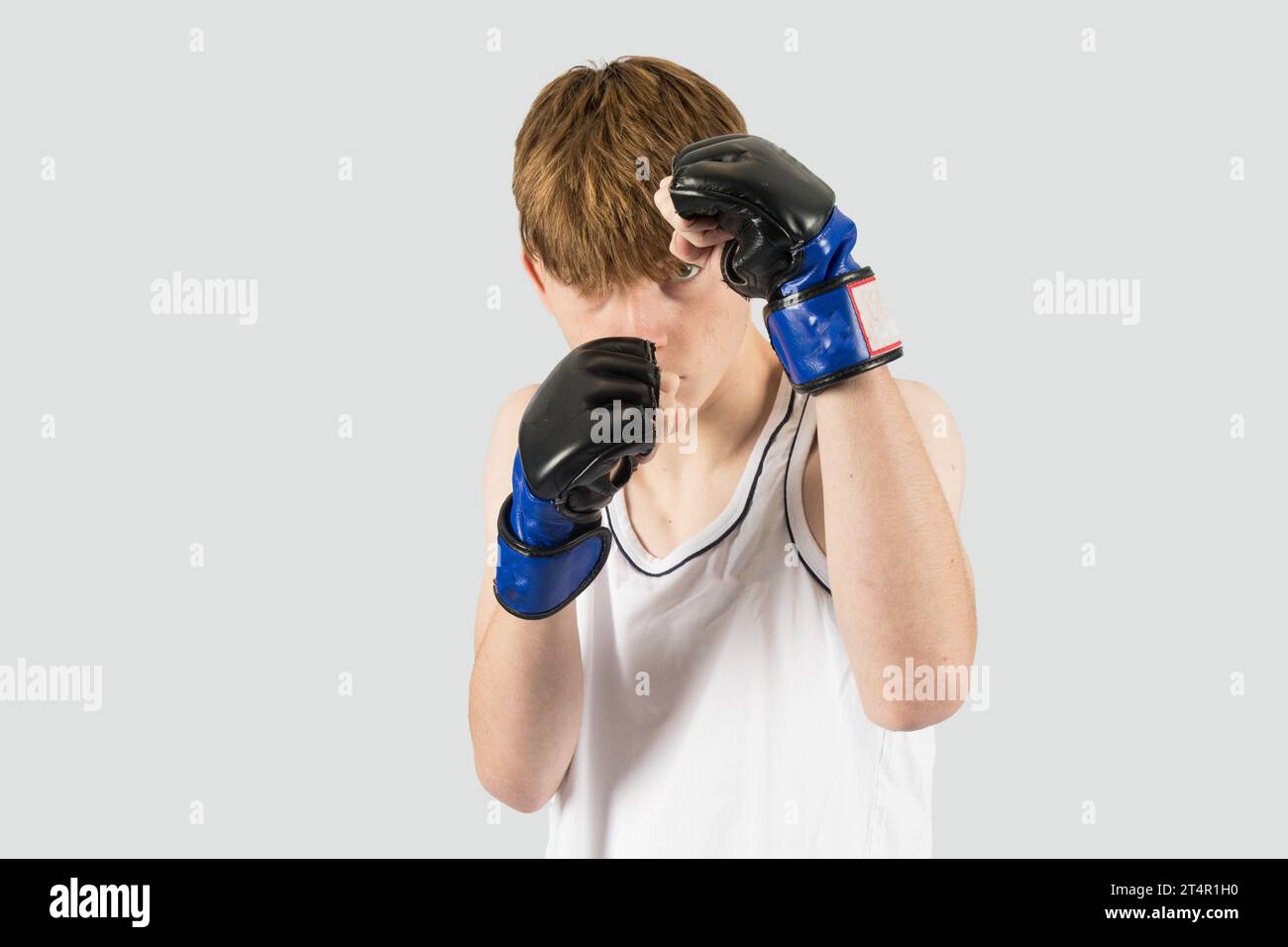 A caucasian teenage boy wearing MMA style boxing gloves with his guard ...