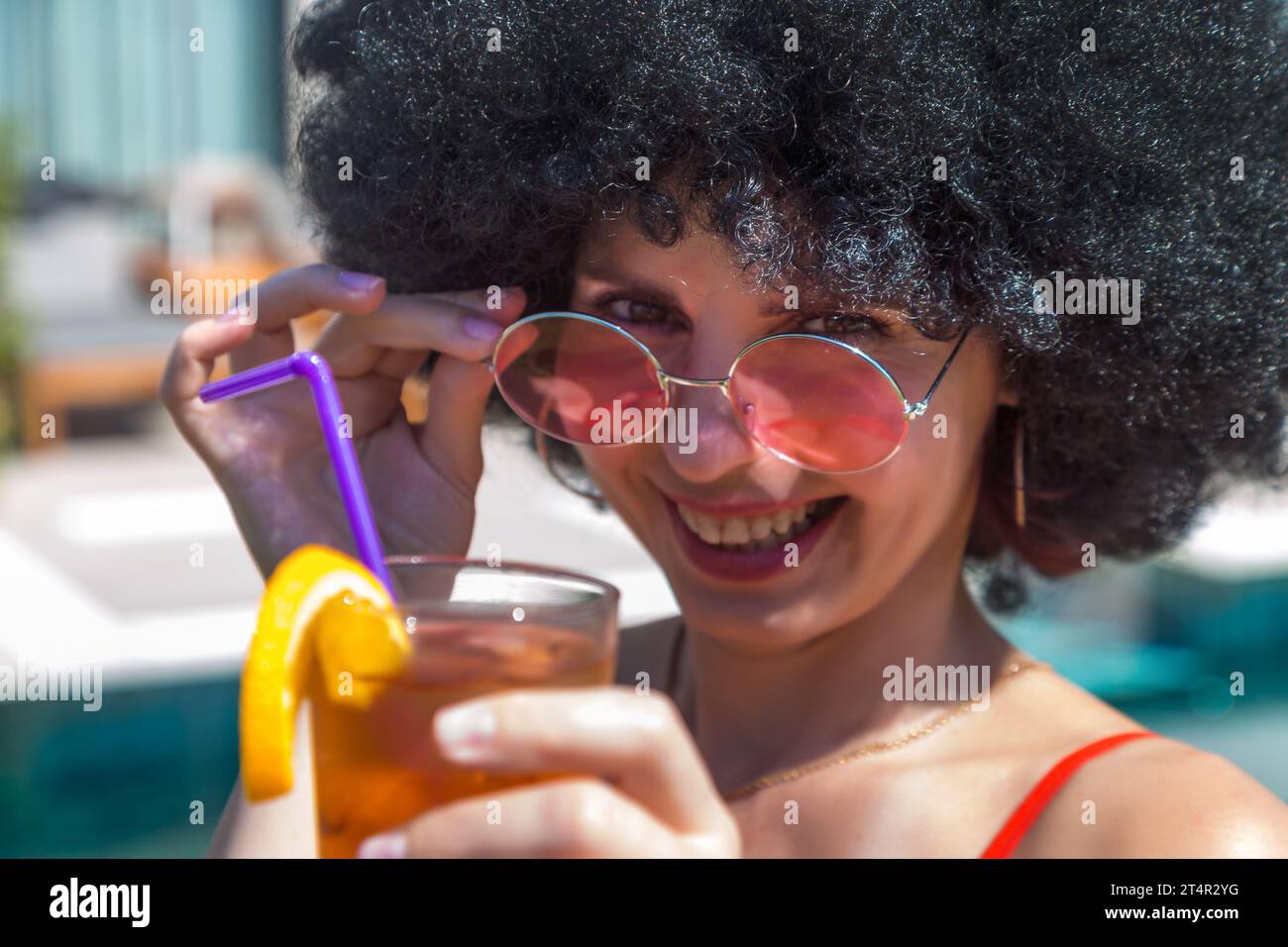 A cheerful girl with black curly hair drinks cocktail with pleasure ...