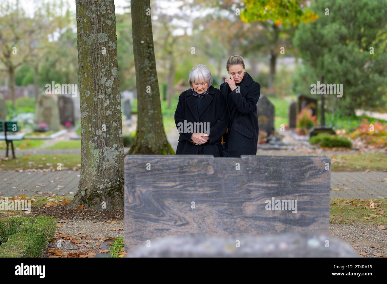 Mother and daughter standing at the man's grave in the cemetery on a ...