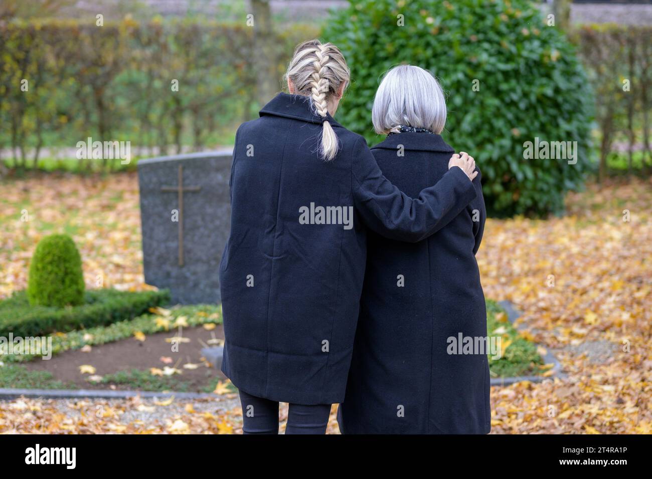 Daughter hugging her mother at the man's grave in the cemetery on a ...