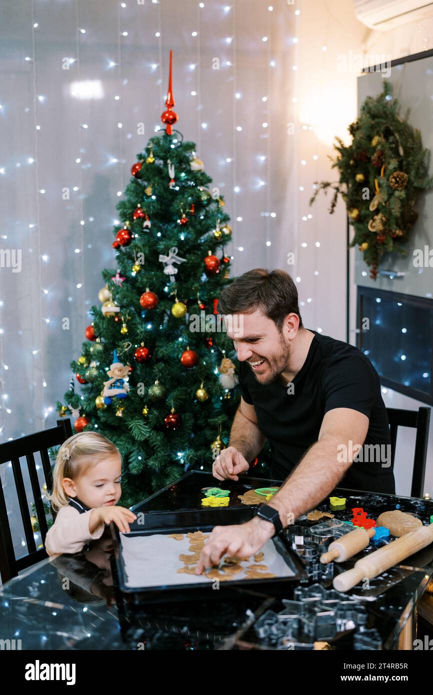 Smiling dad with little daughter laying out Christmas raw cookies on a ...
