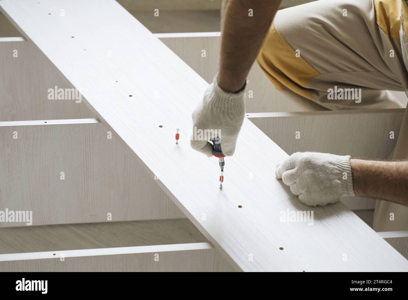 A male worker tightens fasteners on parts of cabinet furniture ...