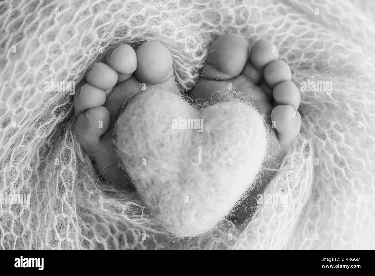 The tiny foot of a newborn baby. Knitted heart in the legs of baby ...