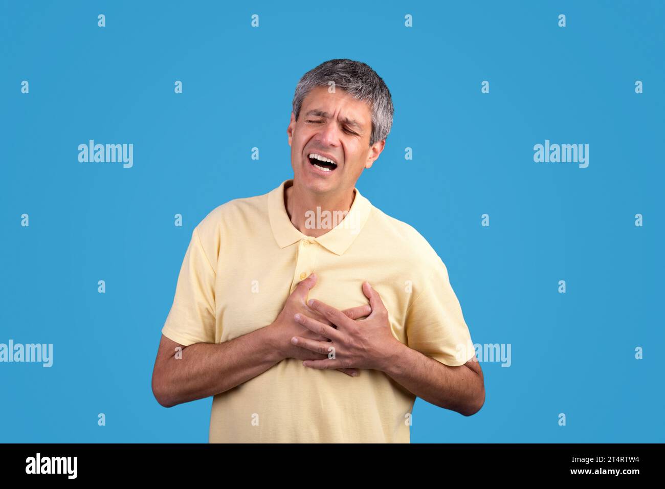 Mature man presses hands to chest expressing pain, blue background ...