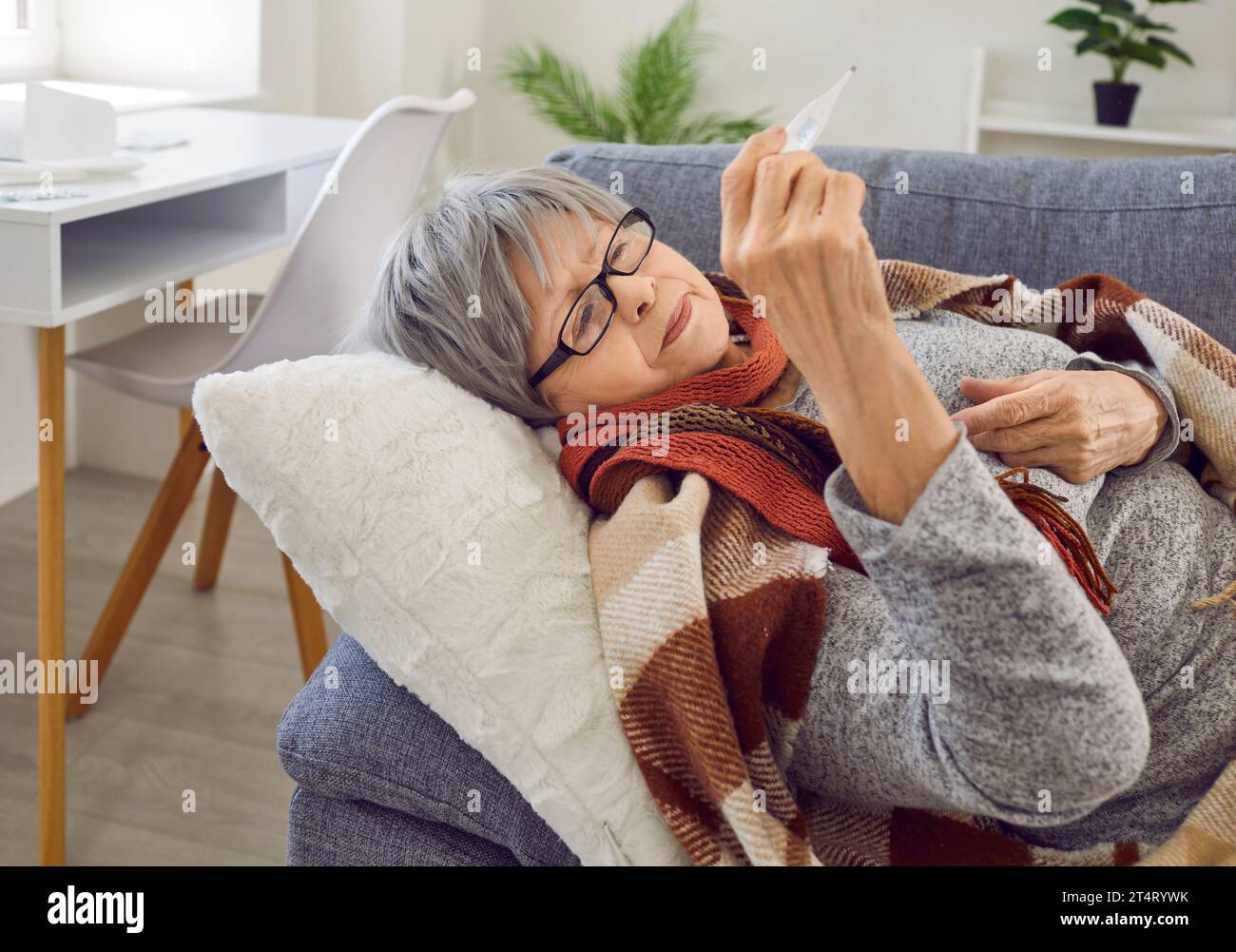 Sick senior woman with flu and fever measures her temperature while ...