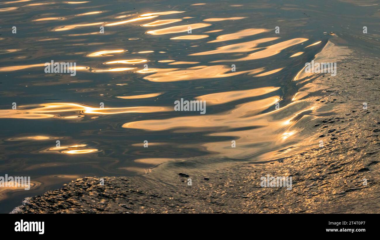 Water ripples and waves reflect the summer sun made hazy and dark by ...