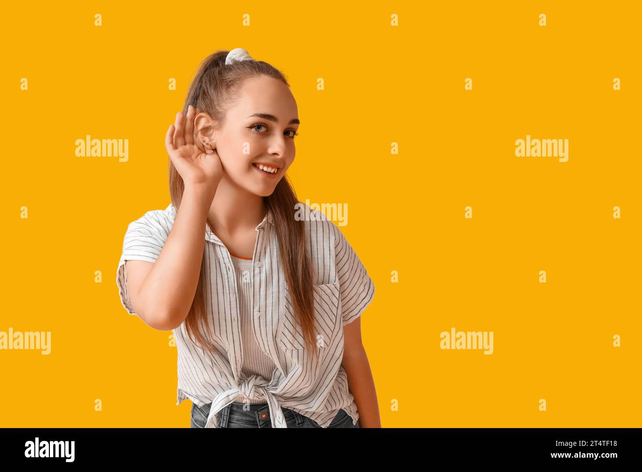 Teenage girl trying to hear something on yellow background Stock Photo ...