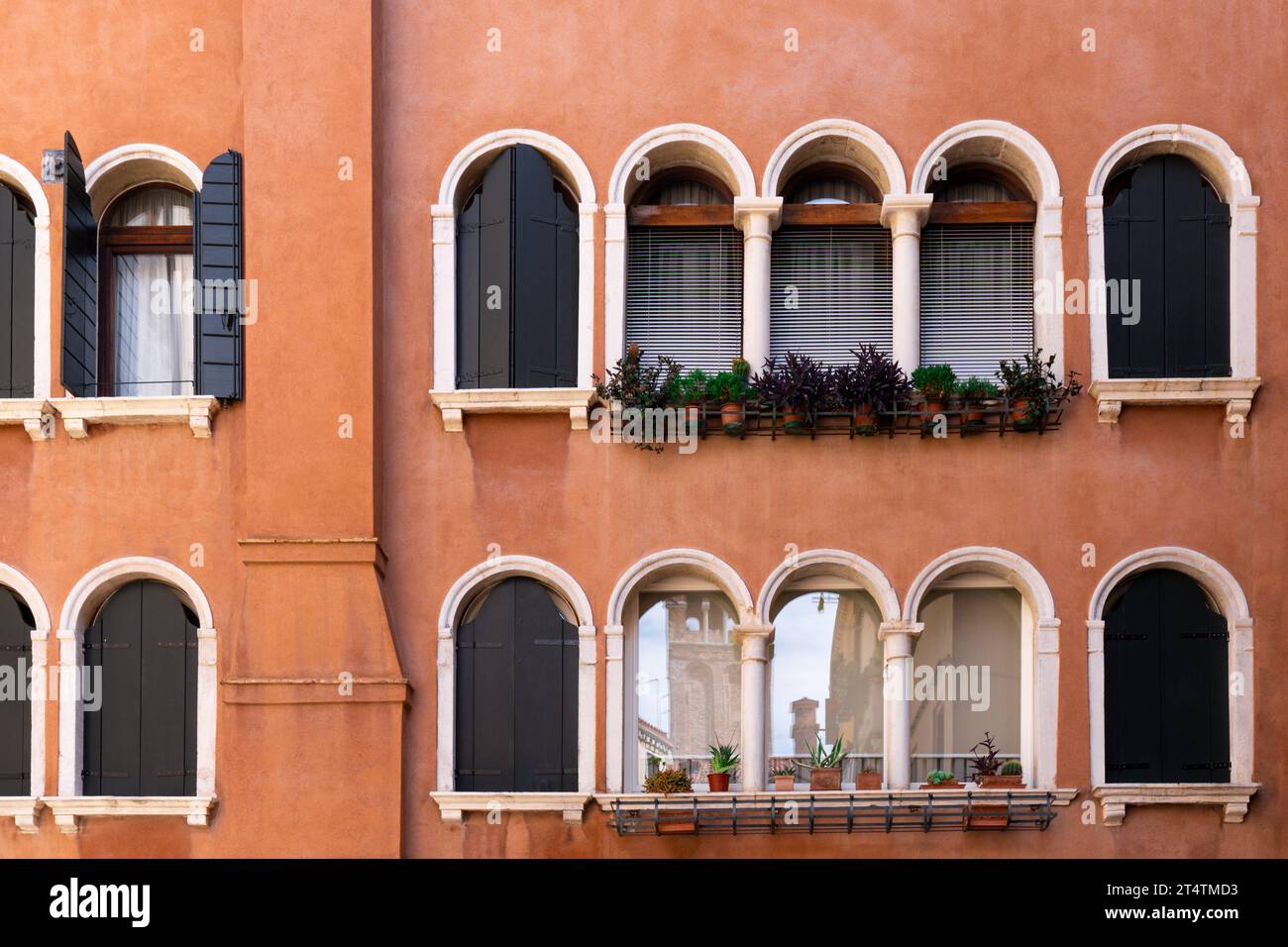 Vintage arched windows with potted plants. Orange color wall building ...