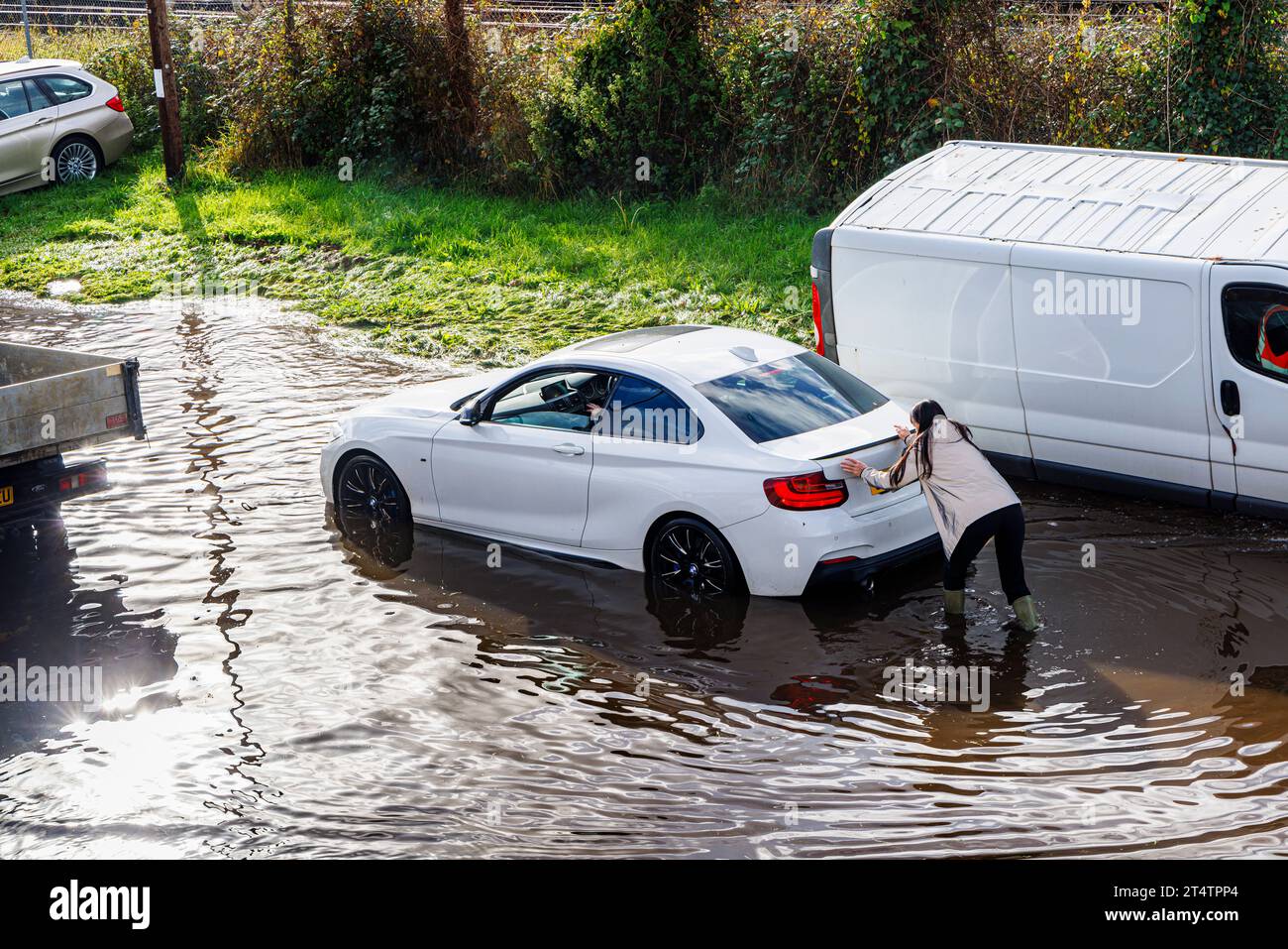 A woman pushes a broken down white BMW car stranded in a flooded road ...