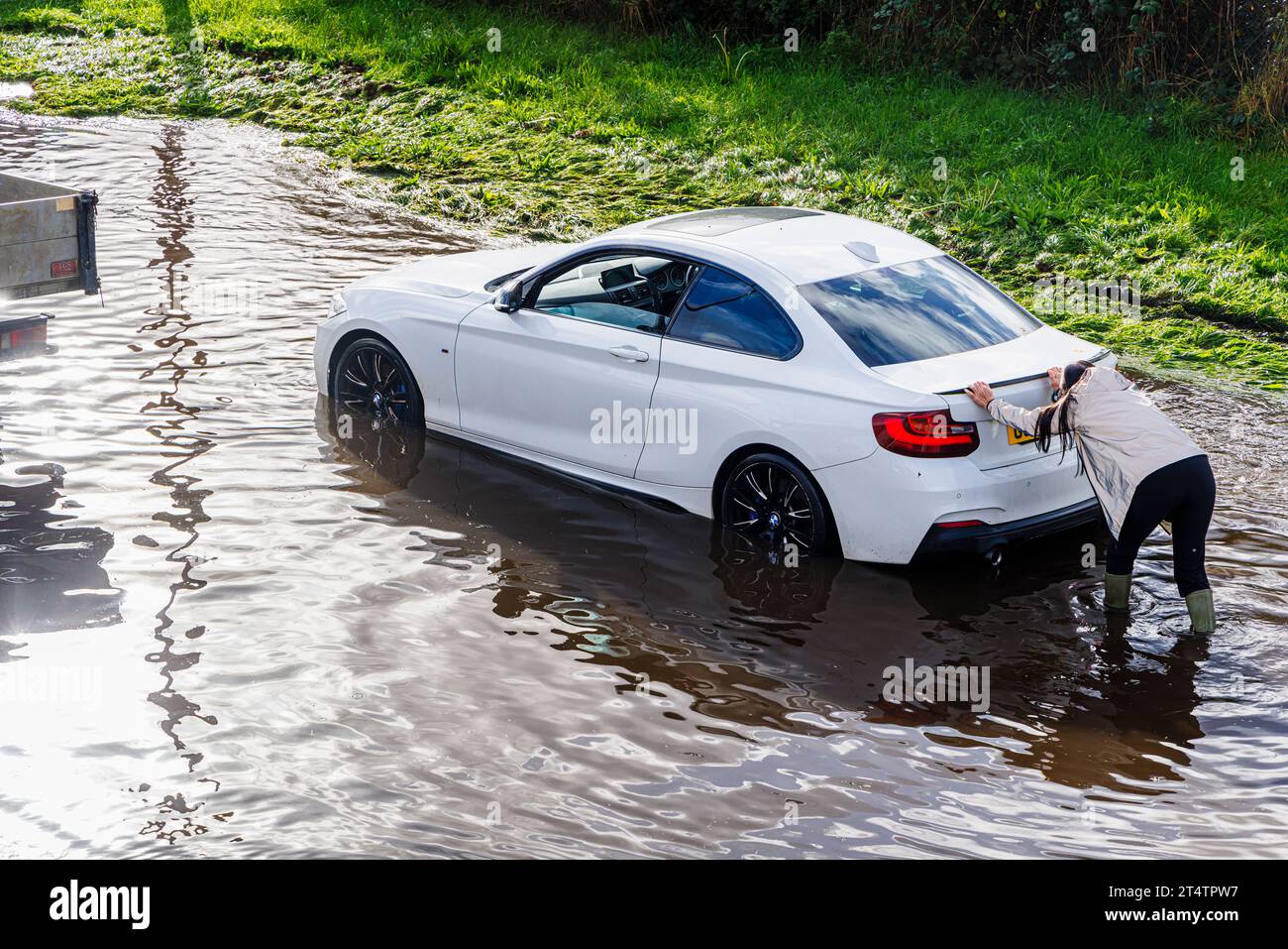 A woman pushes a broken down white BMW car stranded in a flooded road ...