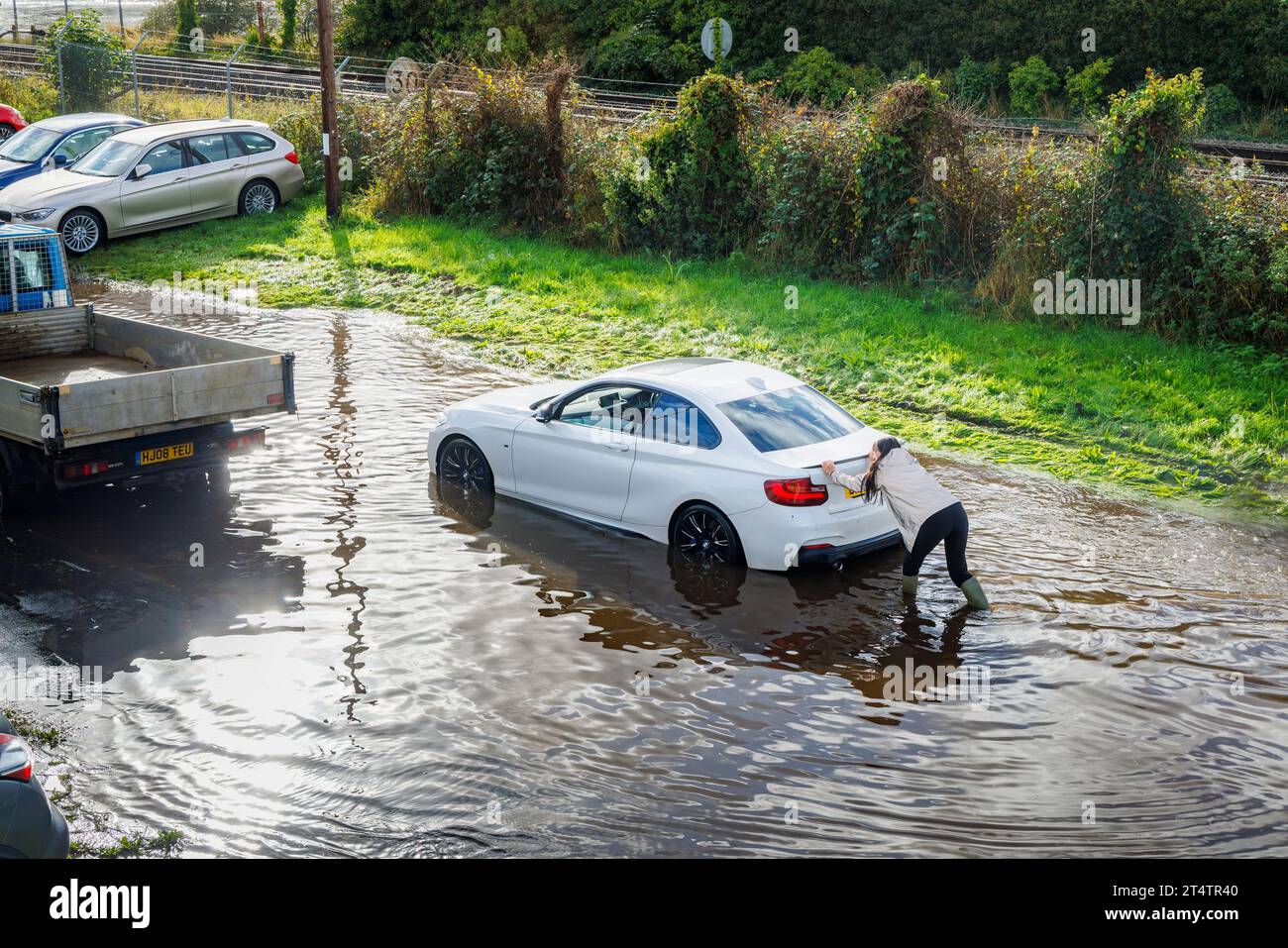 A woman pushes a broken down white BMW car stranded in a flooded road ...