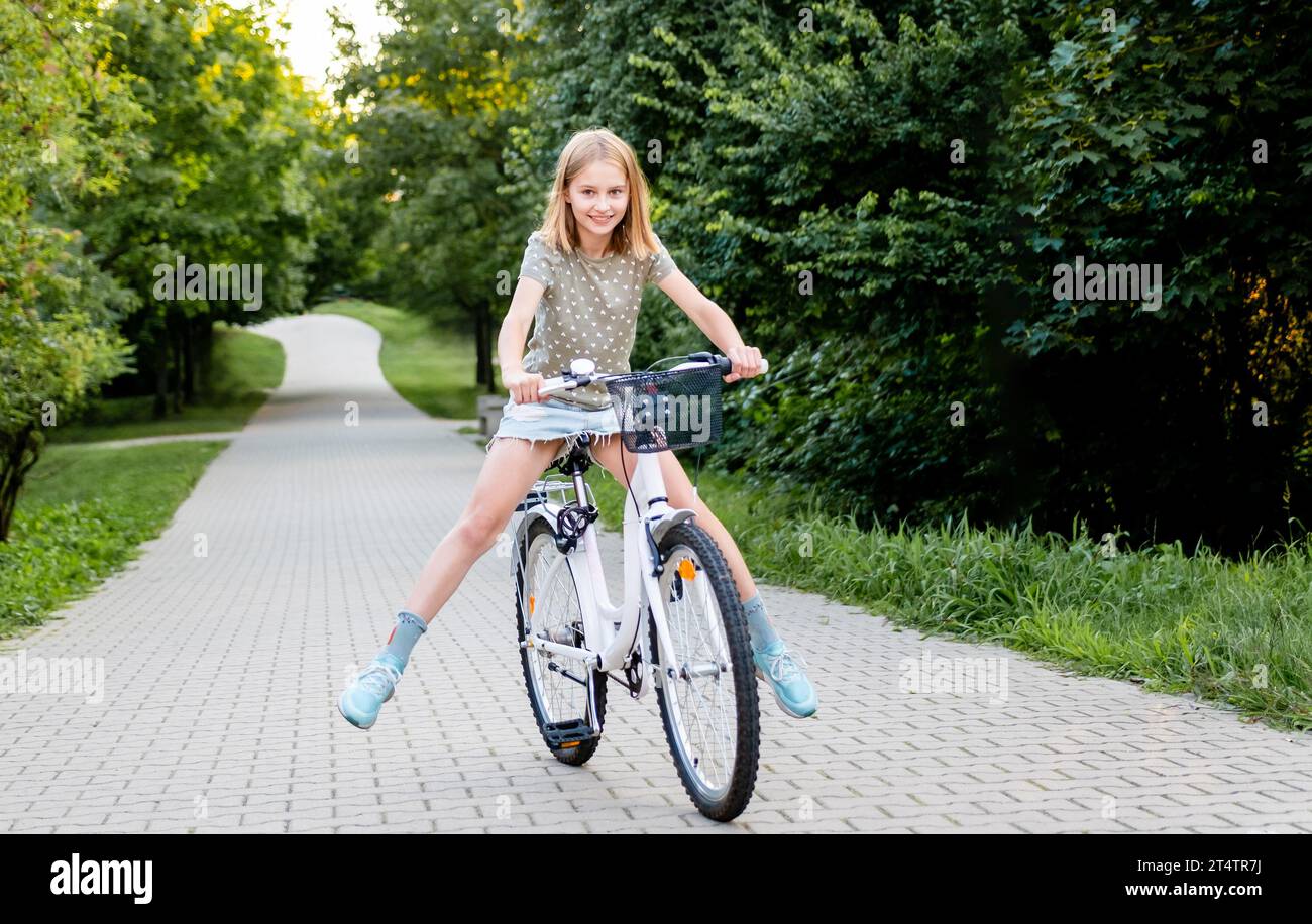 Cute preteen girl riding bycicle outdoors and smiling in beautiful park ...
