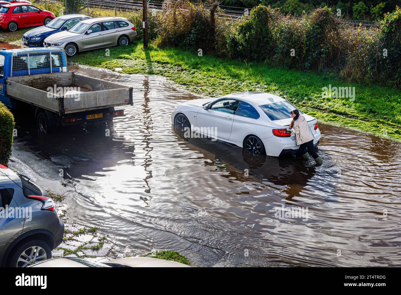 A woman pushes a broken down white BMW car stranded in a flooded road after heavy rainfall and ...
