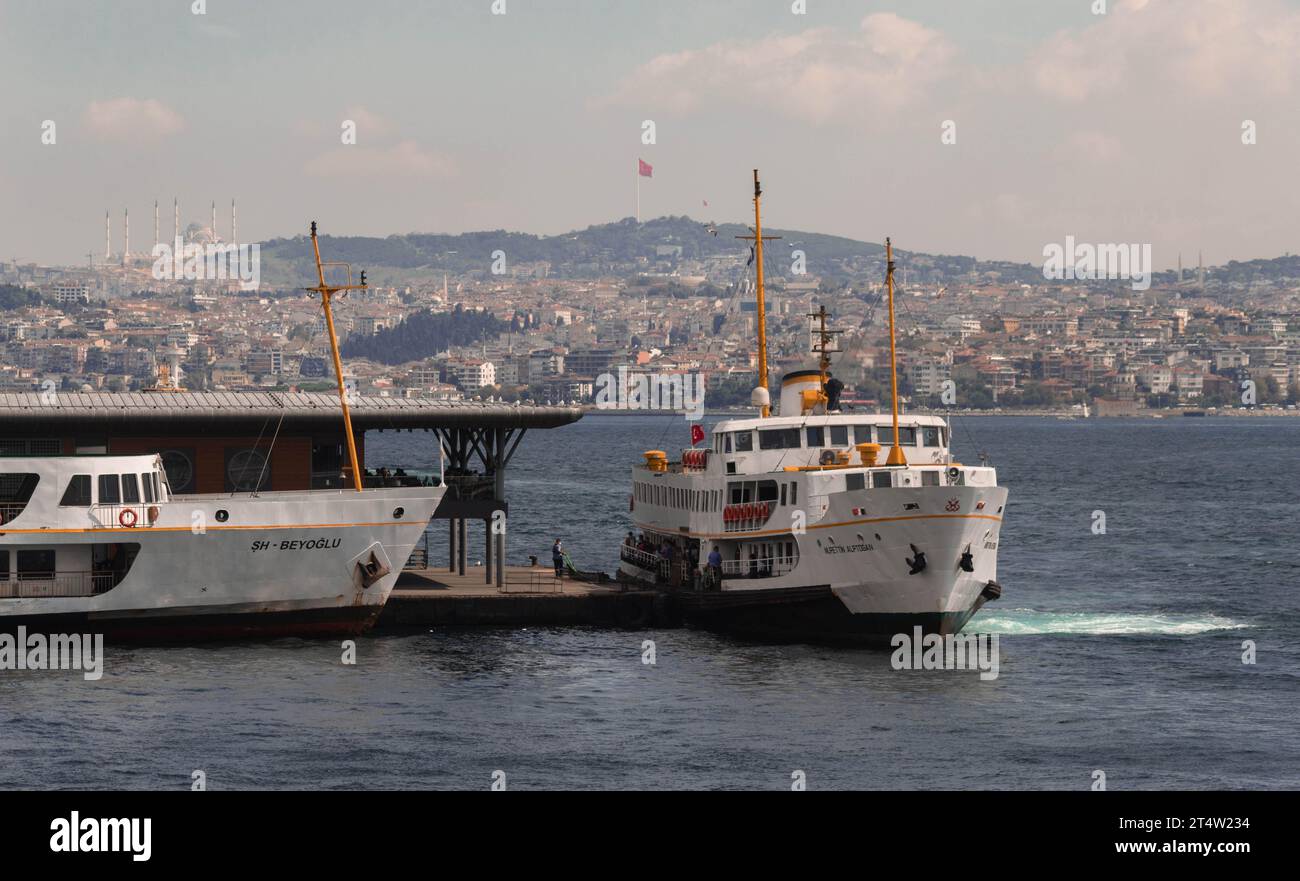 Two ferries at a port in Turkey with a cityscape and hills behind them ...