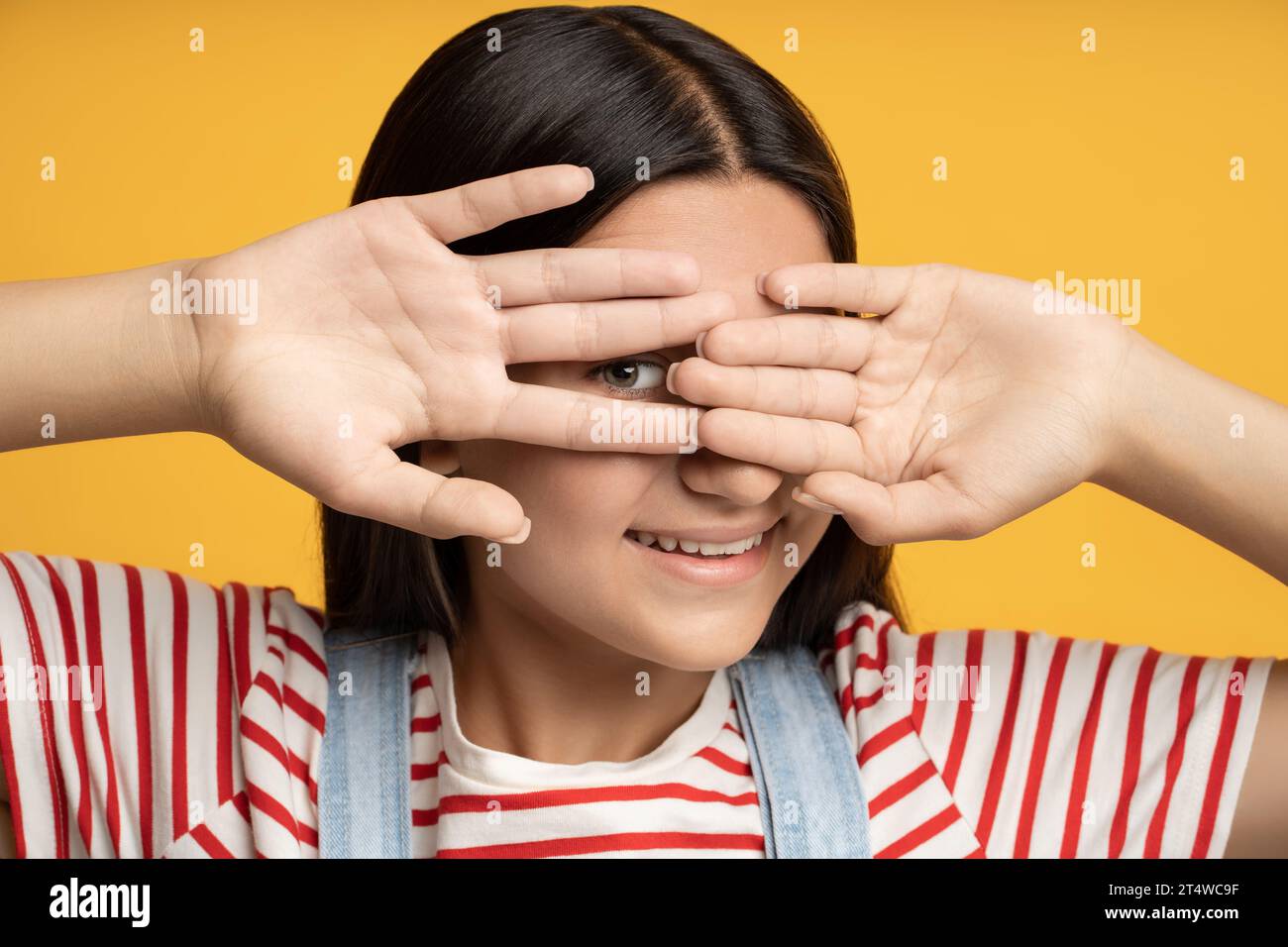 Portrait playful smiling teen girl hiding looking through hand one eye ...