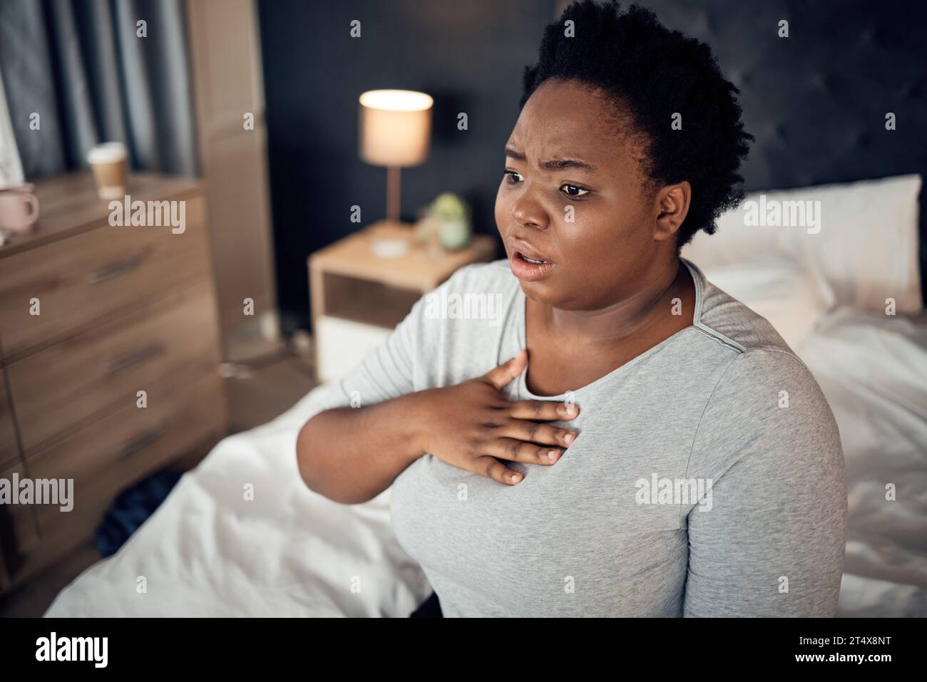 Fear, bedroom and black woman with an anxiety attack or pain in chest from stress. Scary, health ...