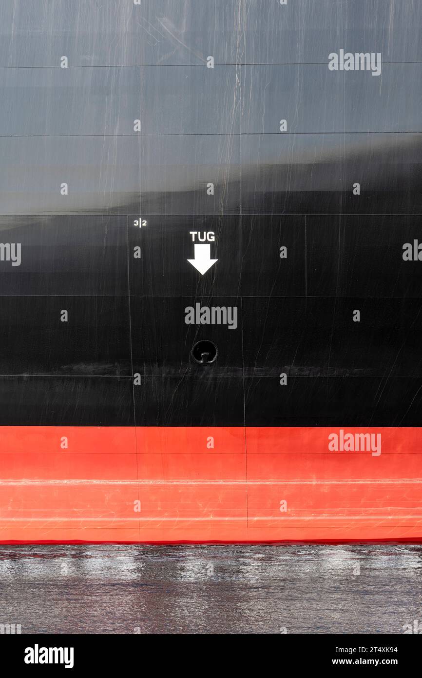 Section of the black and red hull of a ship with letters TUG and arrow ...