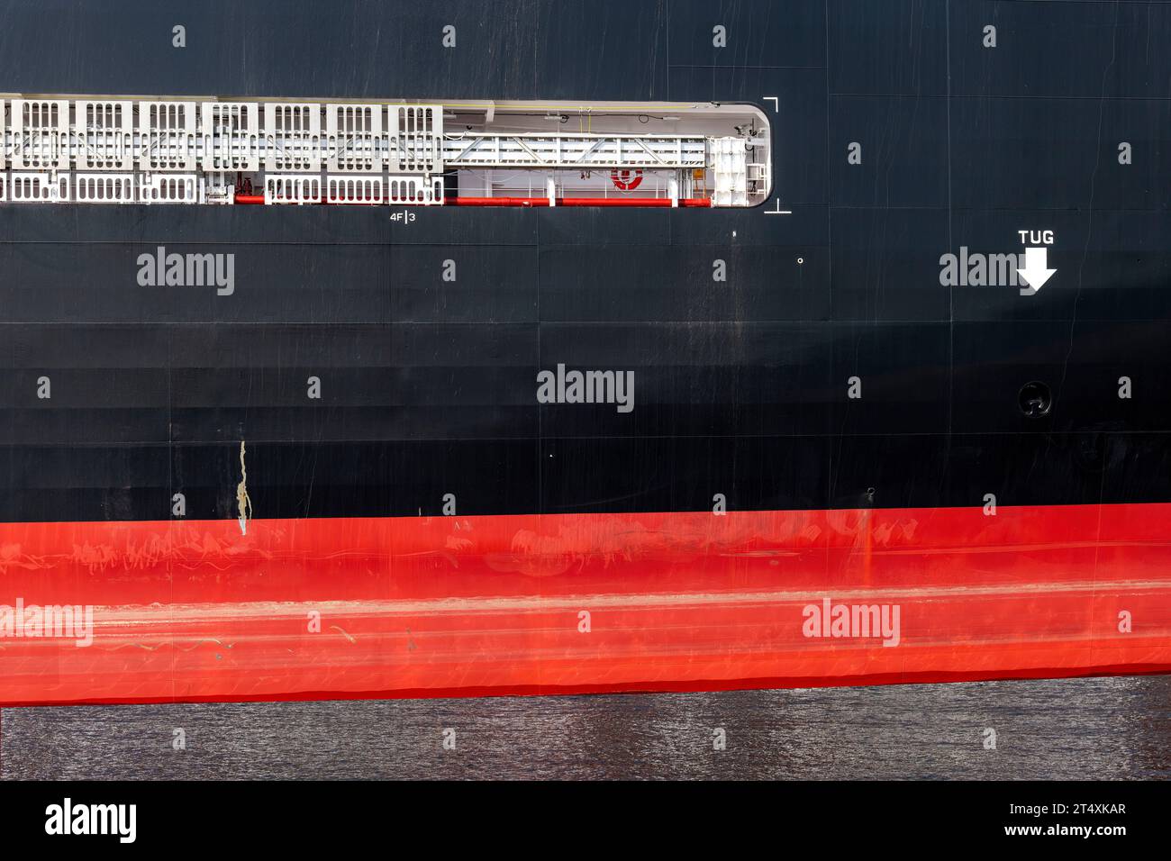 Section of the black and red hull of a ship with letters TUG and arrow ...