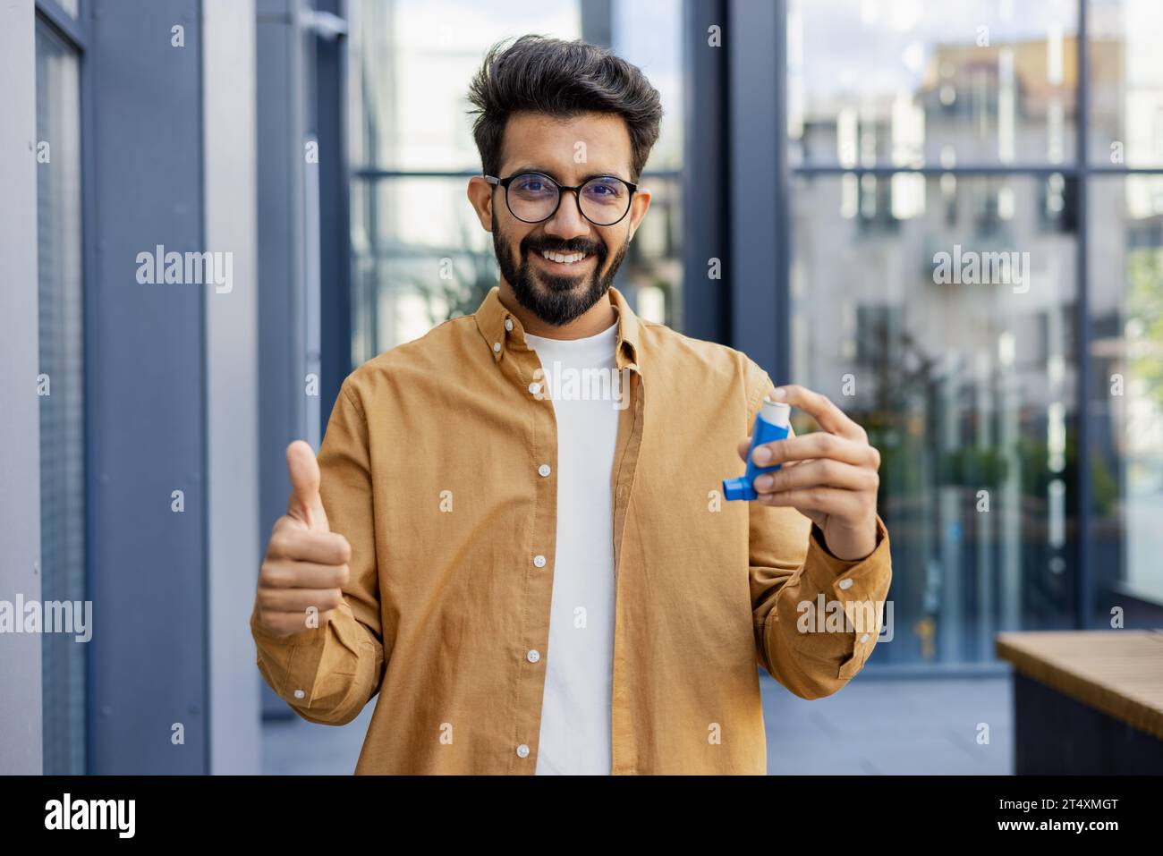 Joyful and smiling man cured, looking at camera showing inhaler to ease ...