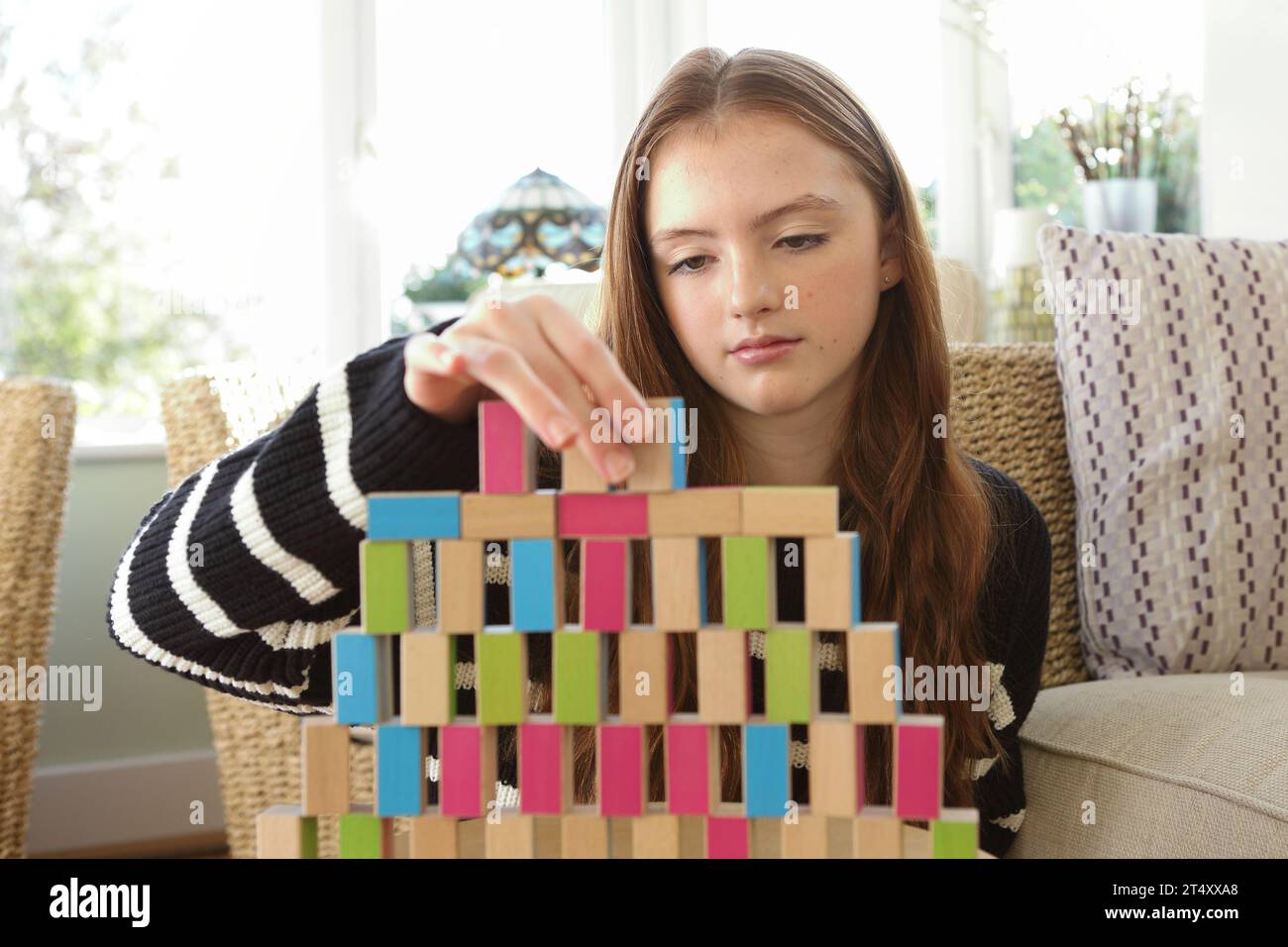 Teenage girl carefully constructing a wall of coloured wooden blocks ...