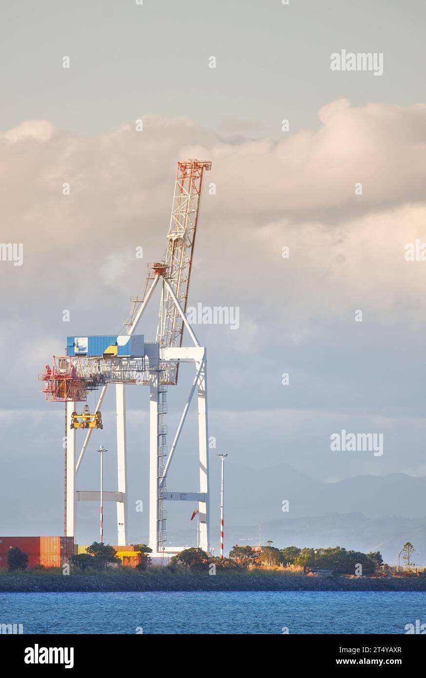 A crane and shipping containers in a shipyard surrounded by the ocean ...