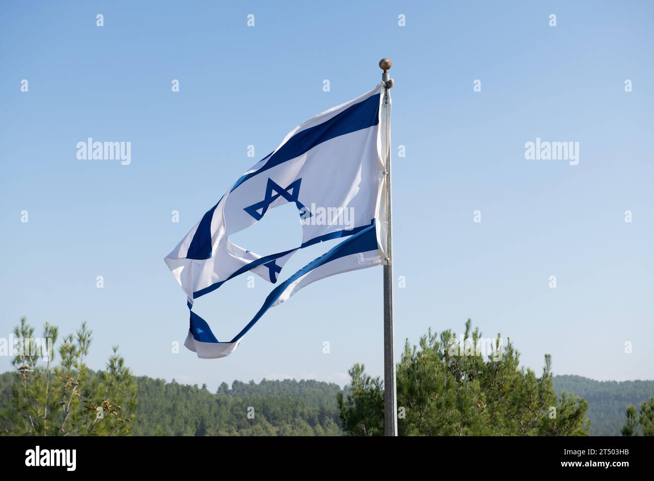 A torn and shredded Israeli flag flutters in the wind at the top of a ...