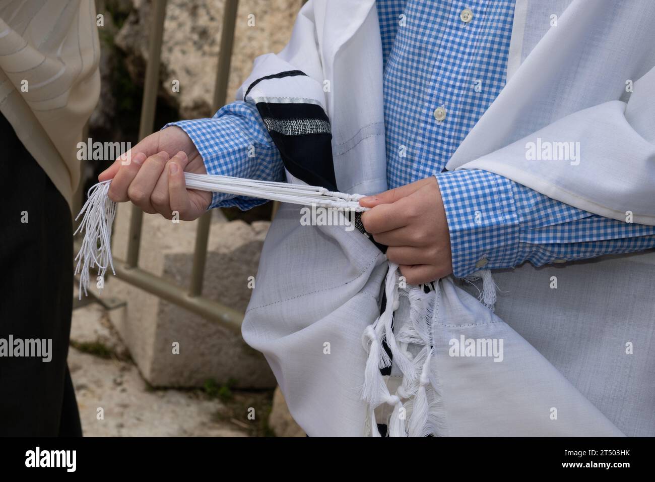A young Jewish man holds the strings of his tallit or tzitzit while ...