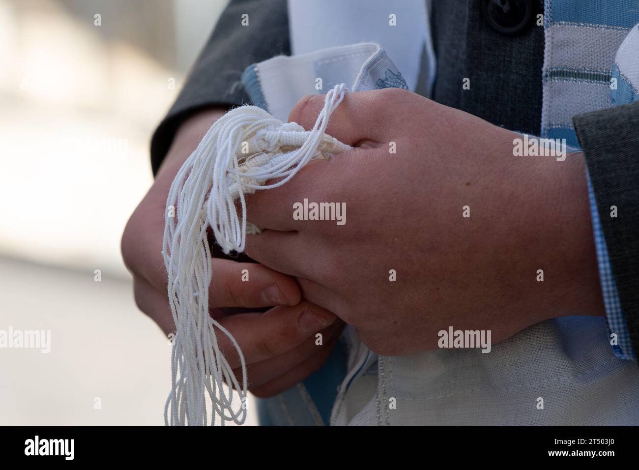 A Jewish man grasps the strings of his tallit or tzitzit while reciting ...