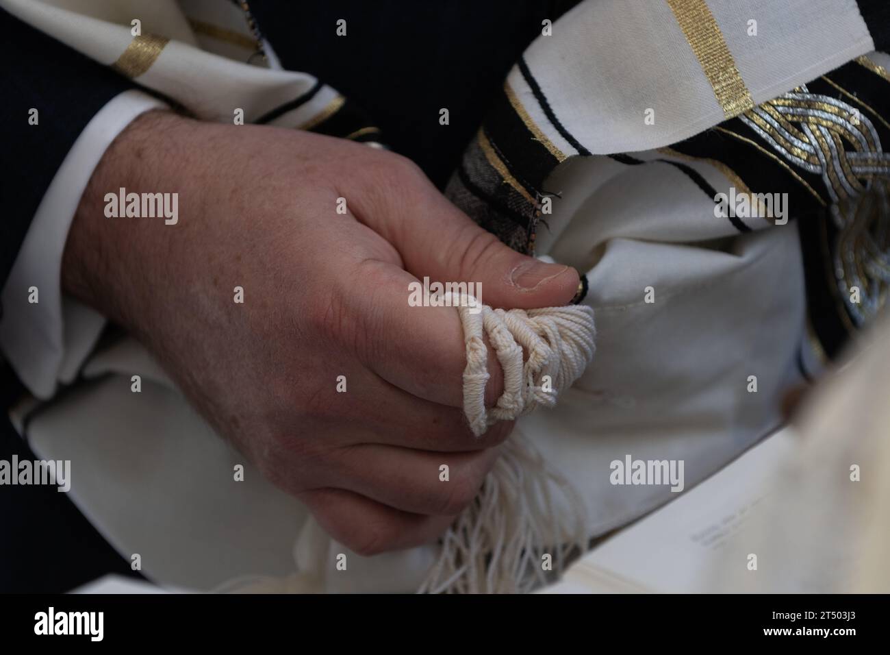 A Jewish man grasps the strings of his tallit or tzitzit while reciting ...