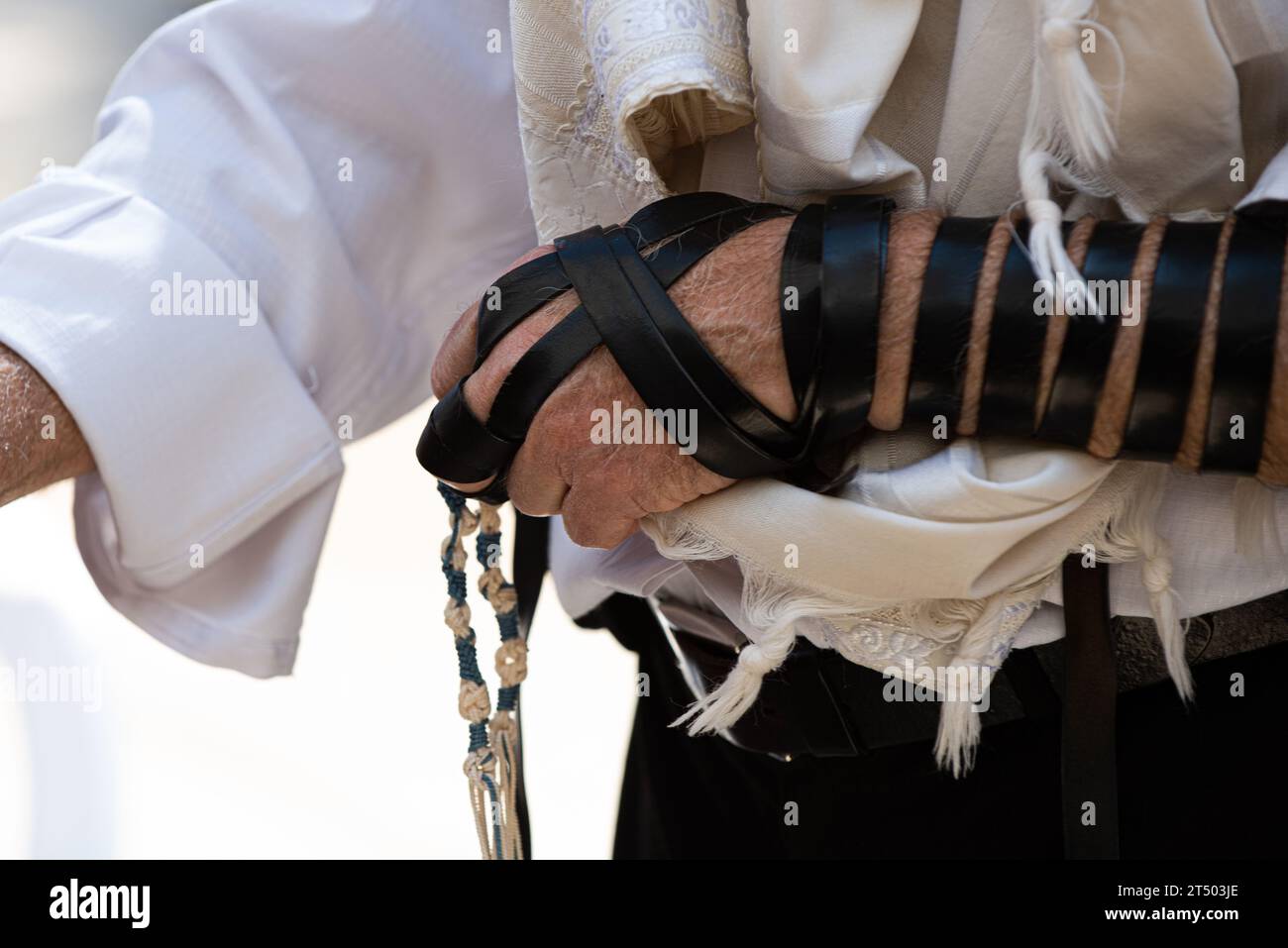 A Jewish man holds the strings of his tallit or tzitzit while reciting ...