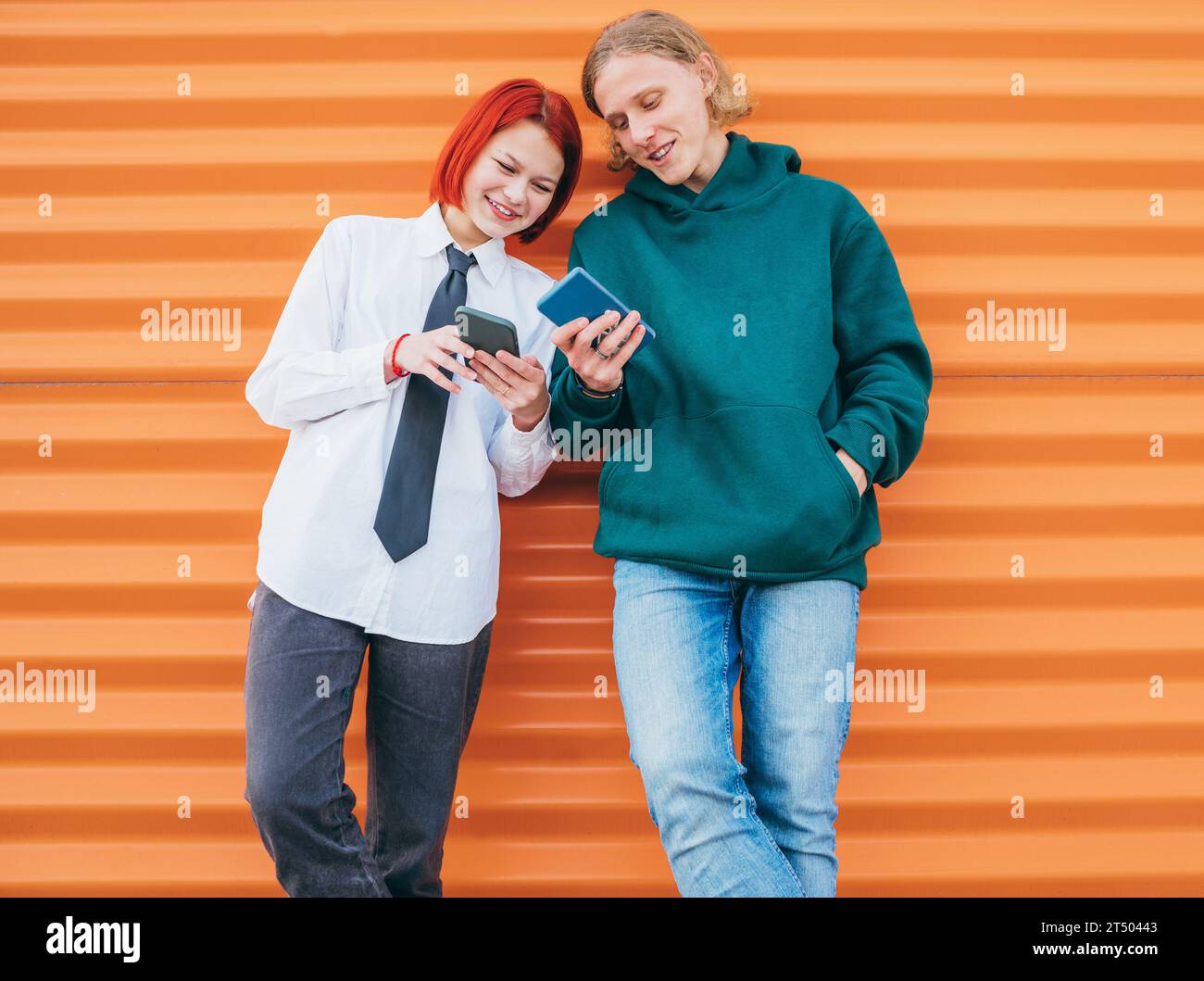 Two caucasian teen friends boy and a girl browsing their smartphone ...