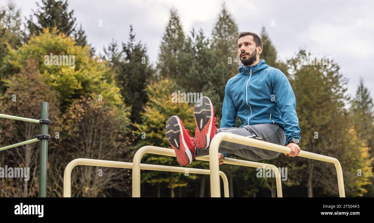 A young athlete trains on the bars, raises his legs parallel to the ...