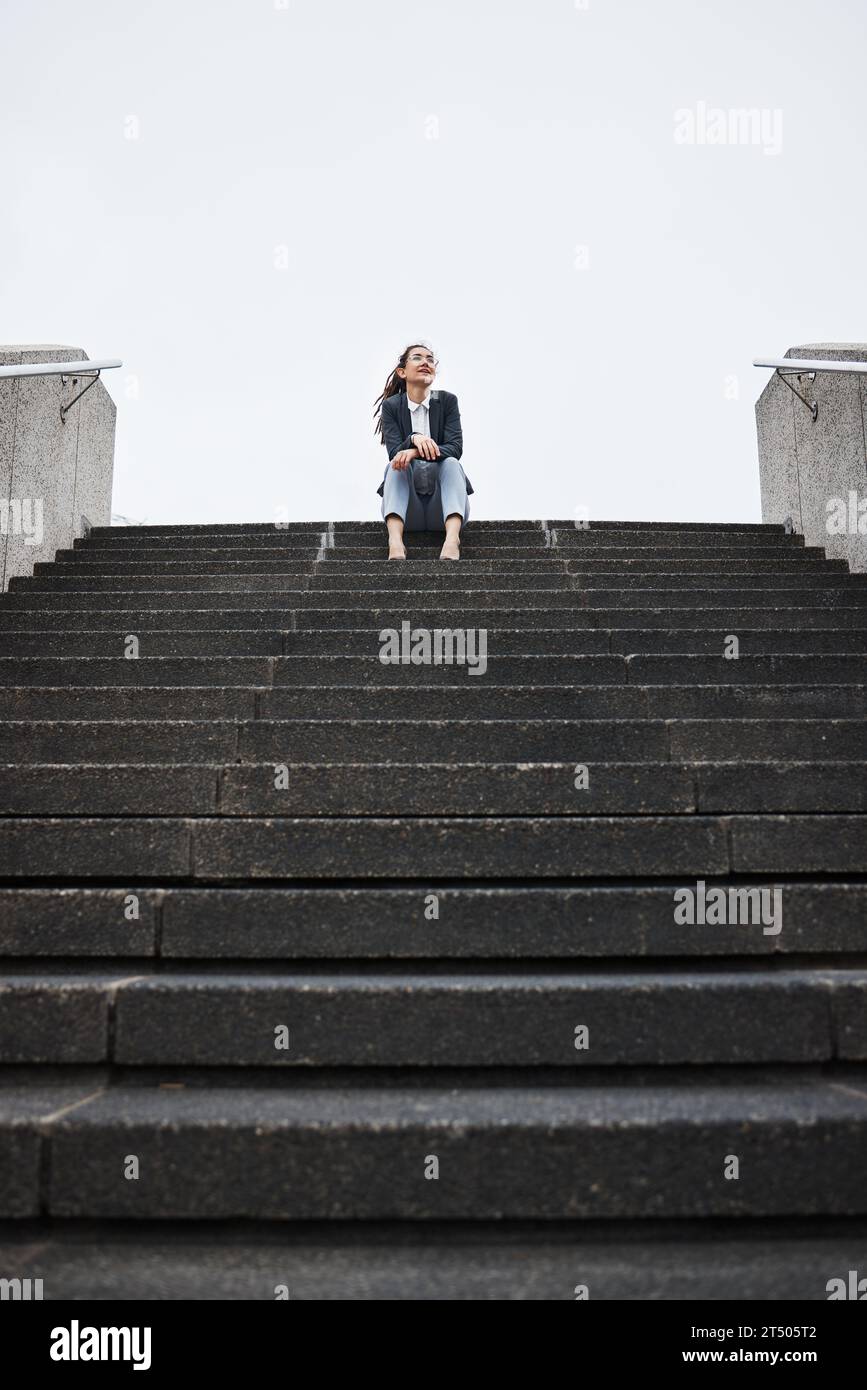 Business woman, city stairs and thinking with sitting, vision and ideas ...