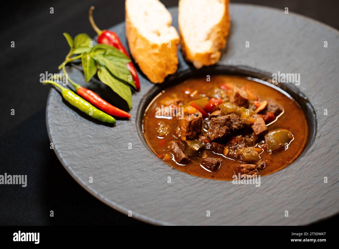 traditional Hungarian food beef goulash with bread an spicy peppers ...