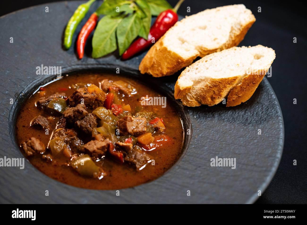 traditional Hungarian food beef goulash with bread an spicy peppers ...