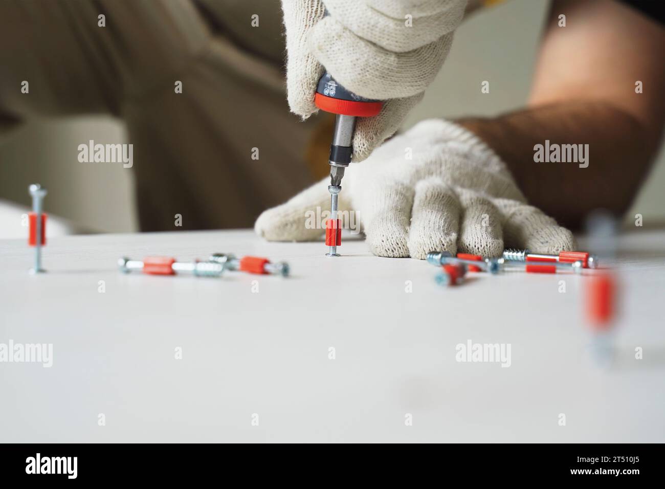 A male worker tightens fasteners on parts of cabinet furniture ...