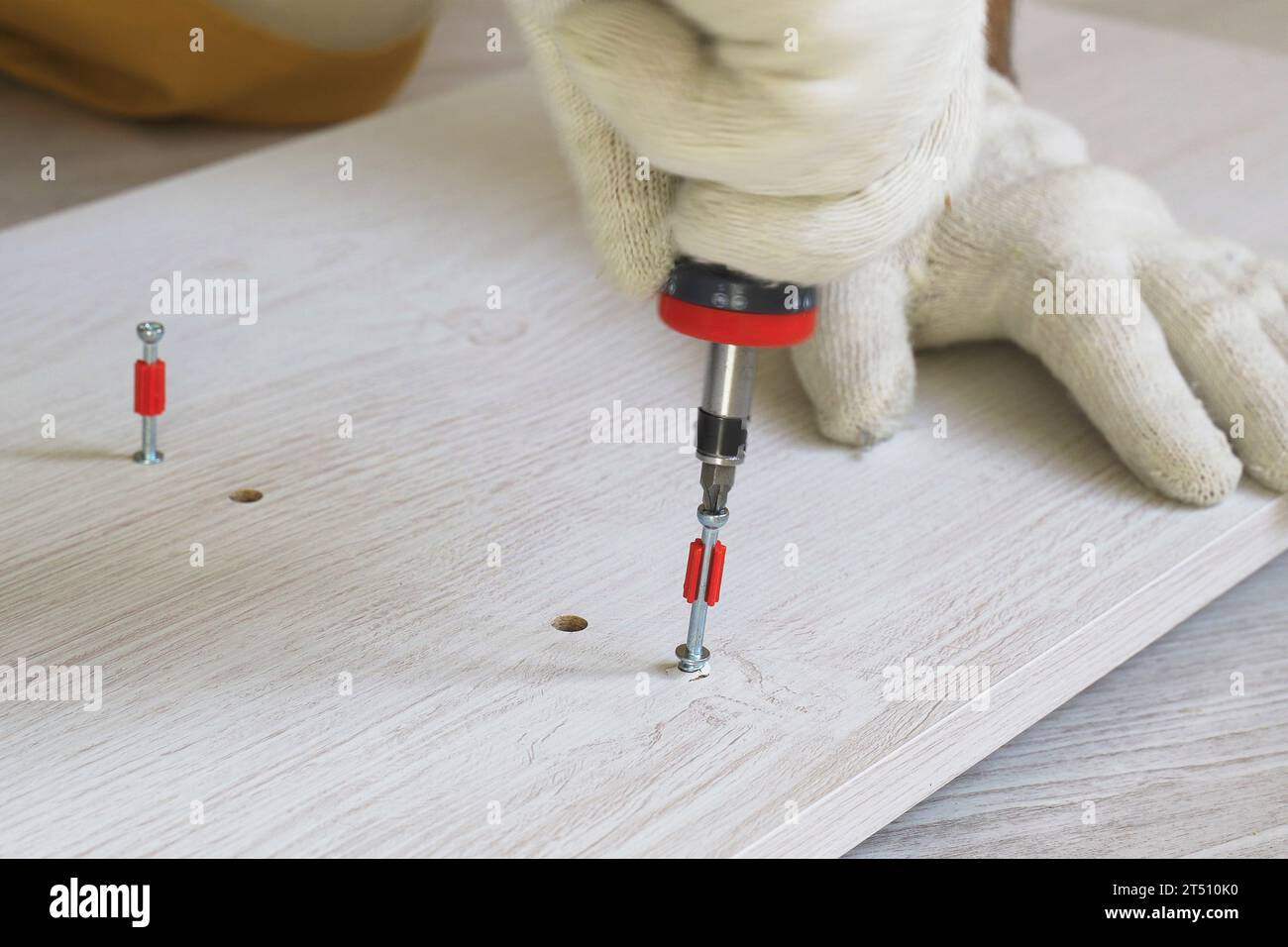A male worker tightens fasteners on parts of cabinet furniture ...