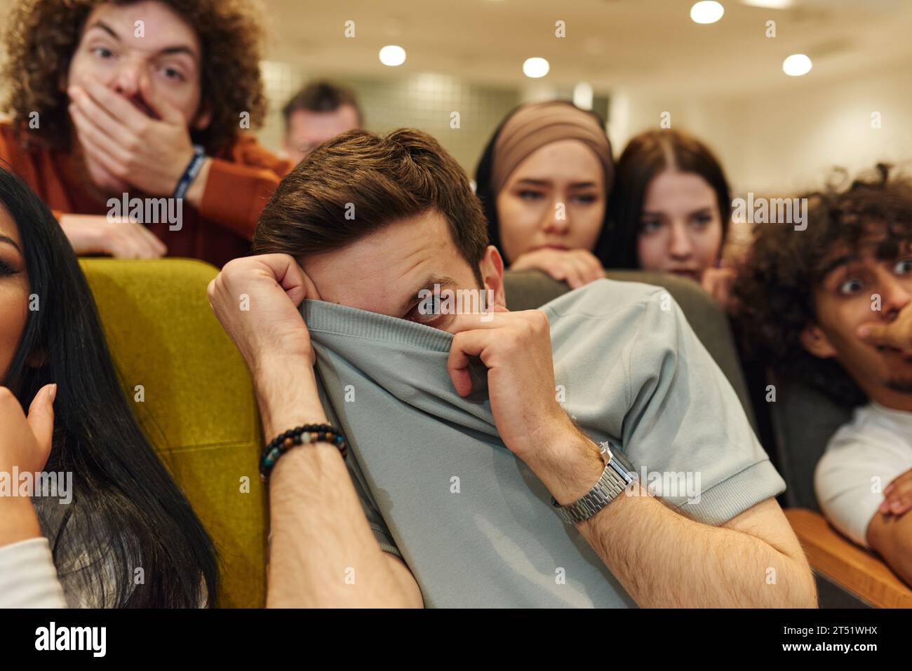 A diverse group of young people watches a thrilling movie in a cinema ...