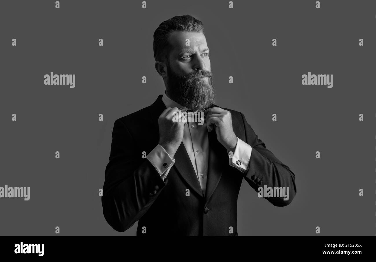 Elegant man fixing bowtie in black tuxedo. Handsome man with red beard ...