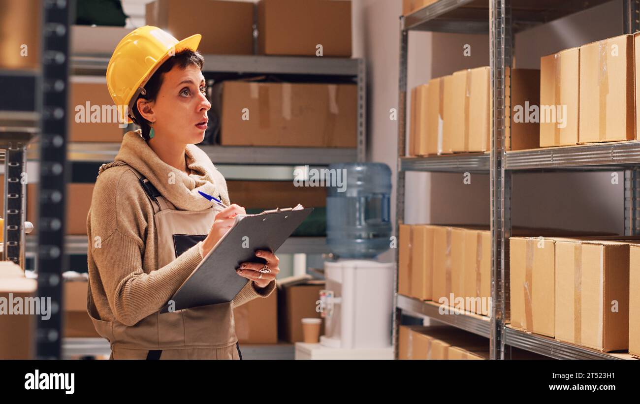 Female employee checking list of products in depot, working on stock ...