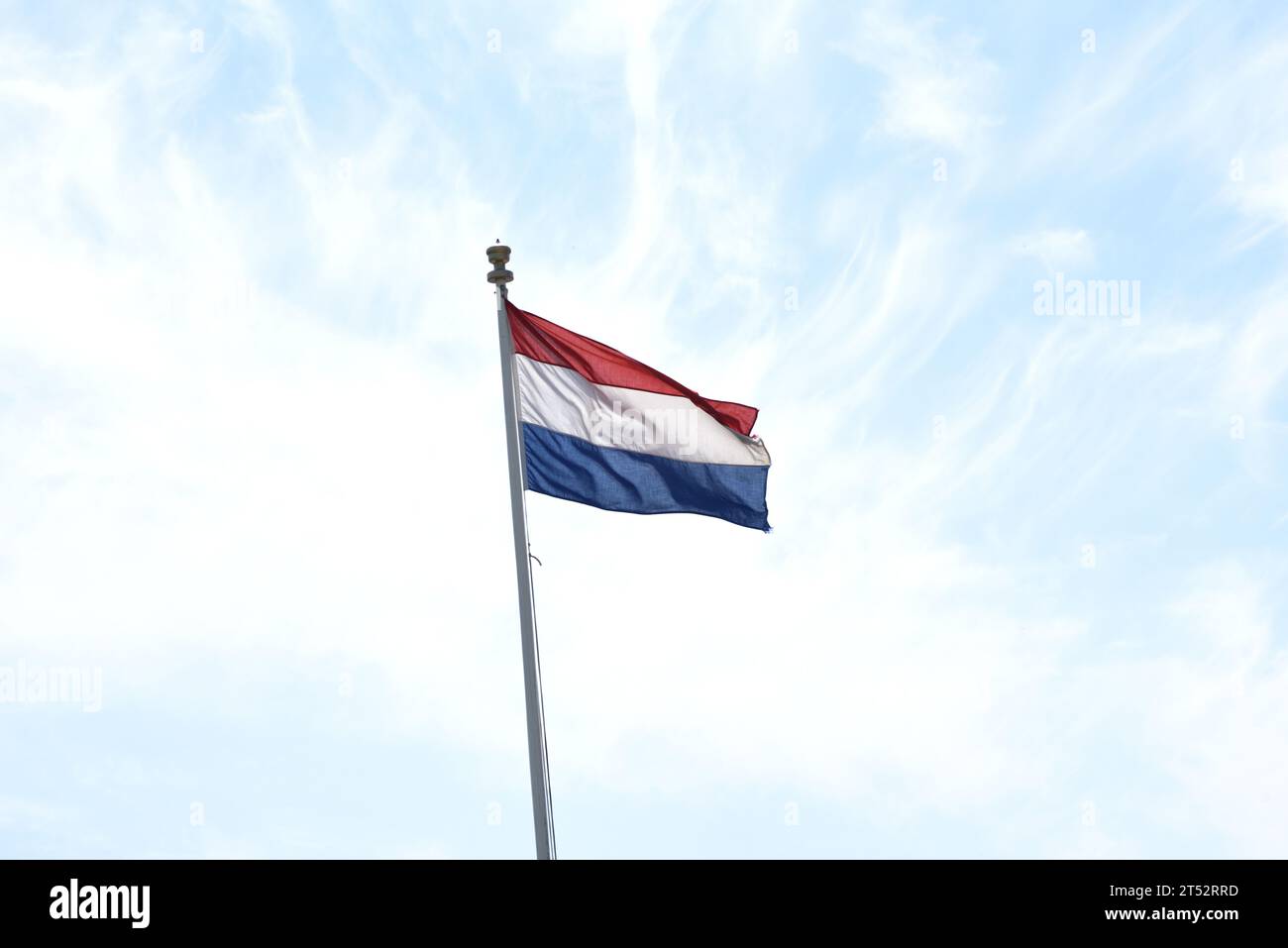 A vibrant flag of Netherlands waving against a clear blue sky depicting ...