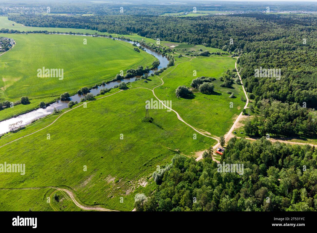 Aerial view of green fields in a river floodplain surrounded by forests ...