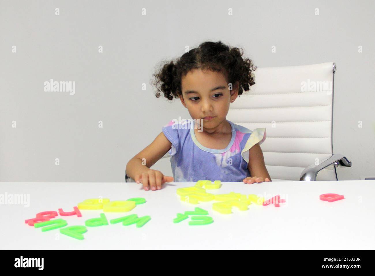 3-year-old Latina girl with brunette and curly hair plays with a game ...