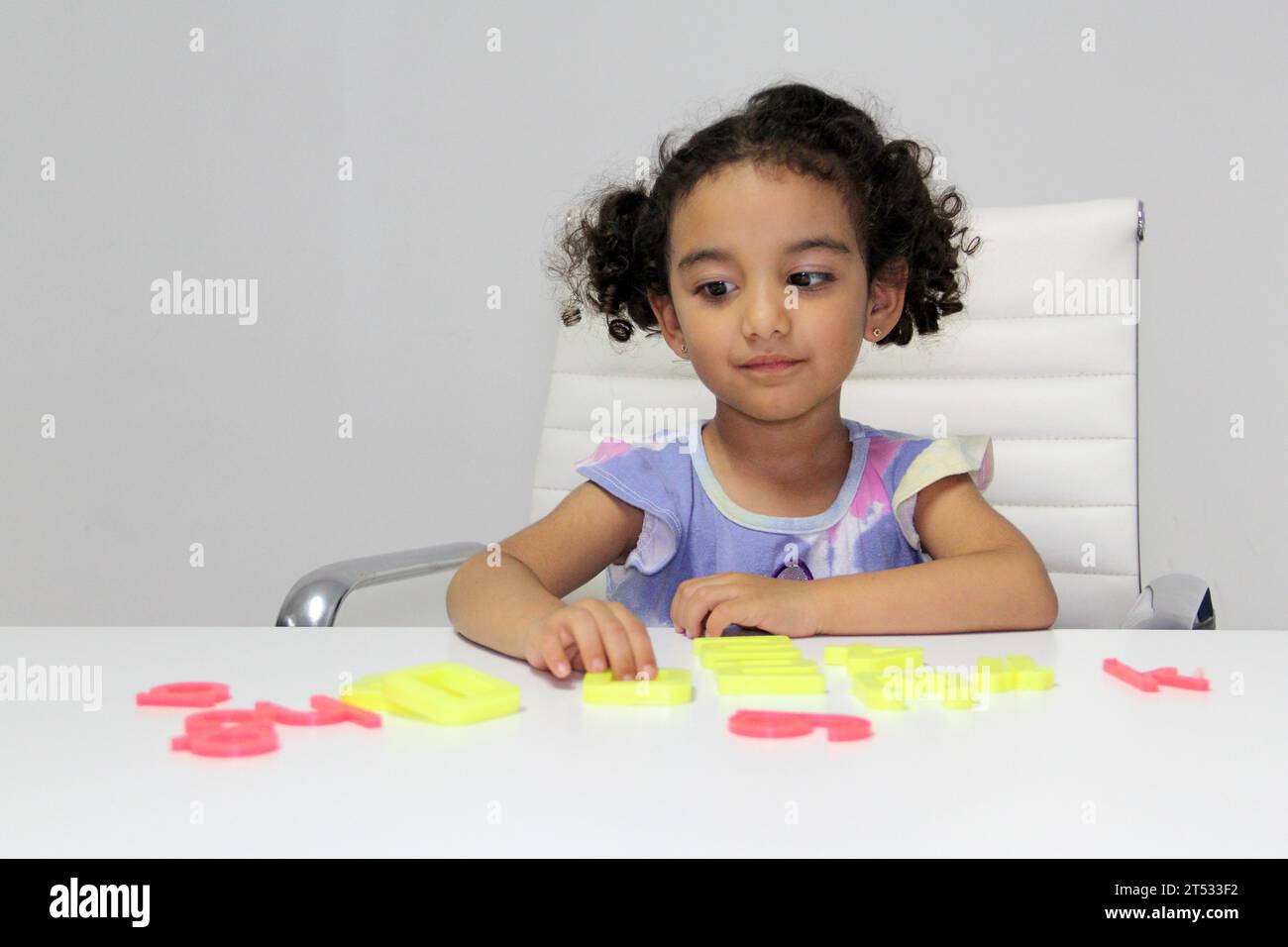 3-year-old Latina girl with brunette and curly hair plays with a game ...