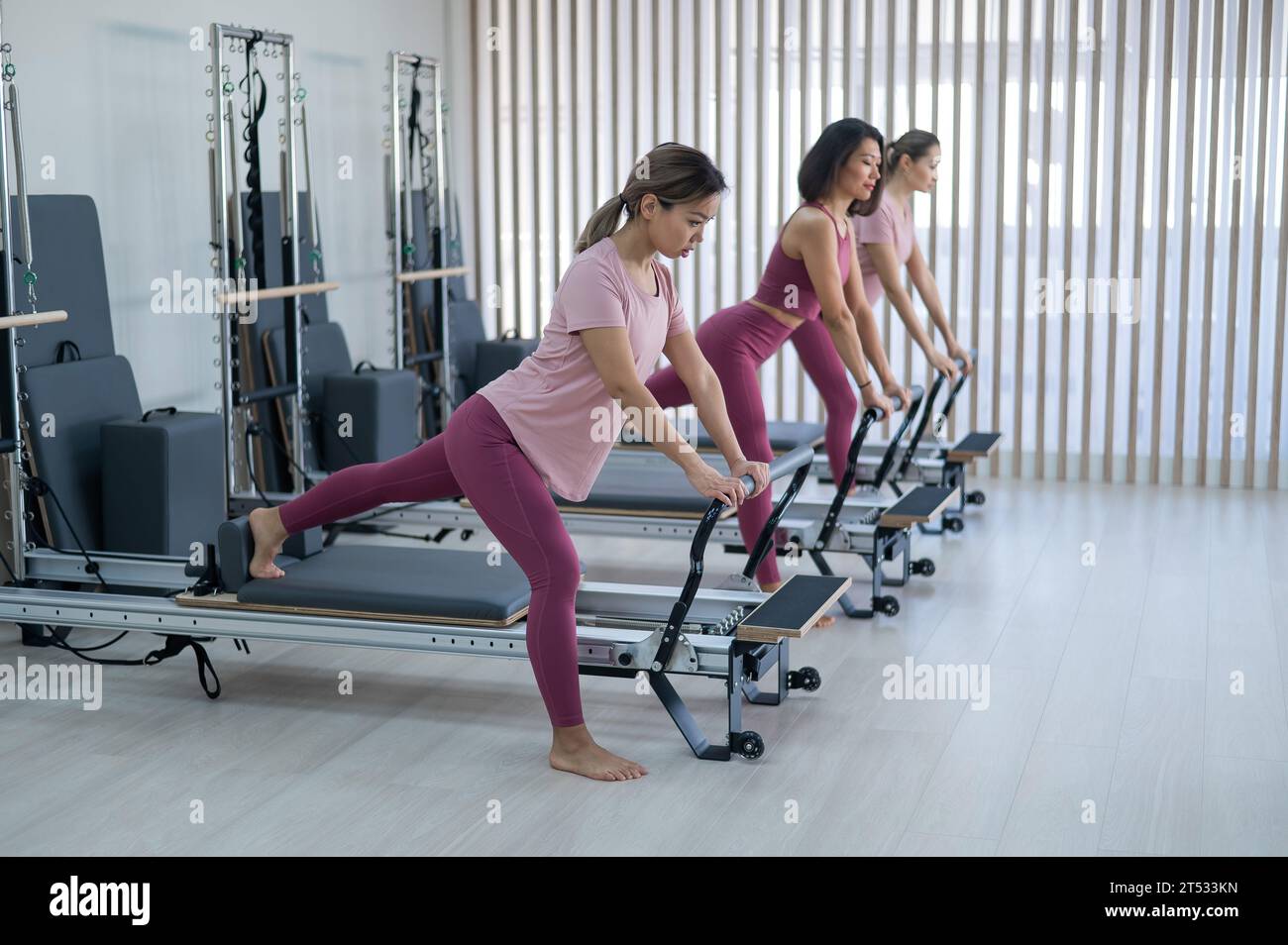 Three Asian women doing lunges on a reformer machine Stock Photo - Alamy
